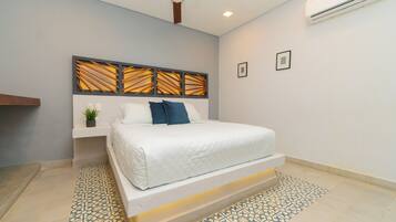 Quarto com cama, ventilador de teto, ar condicionado fixado na parede e painel decorativo.