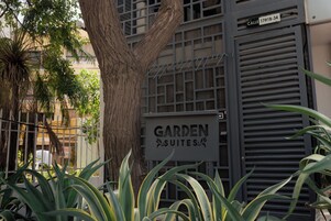 Placa indica 'Garden Suites', com uma árvore e plantas em primeiro plano.