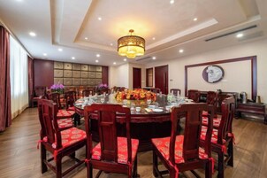 Uma sala de jantar ampla com mesa redonda, cadeiras estofadas em vermelho e um candelabro.