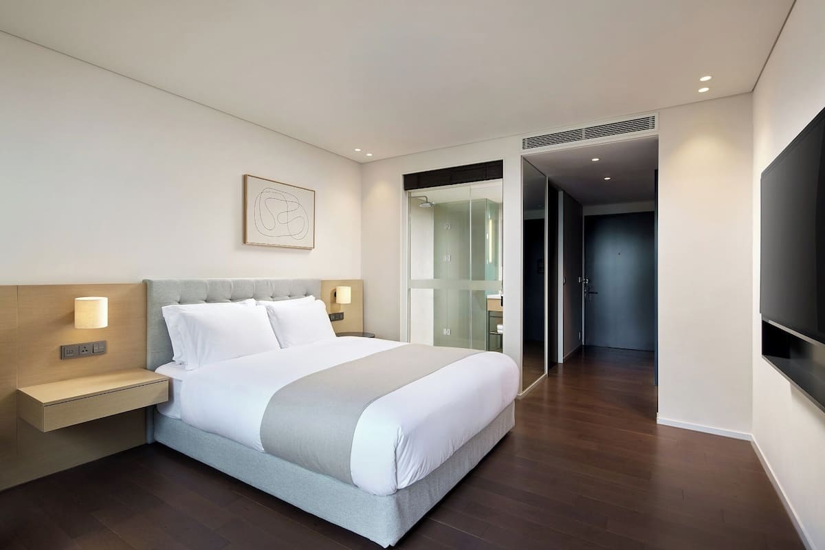 Quarto de hotel moderno com uma cama grande, mesas de cabeceira, uma TV de tela plana e chuveiro.