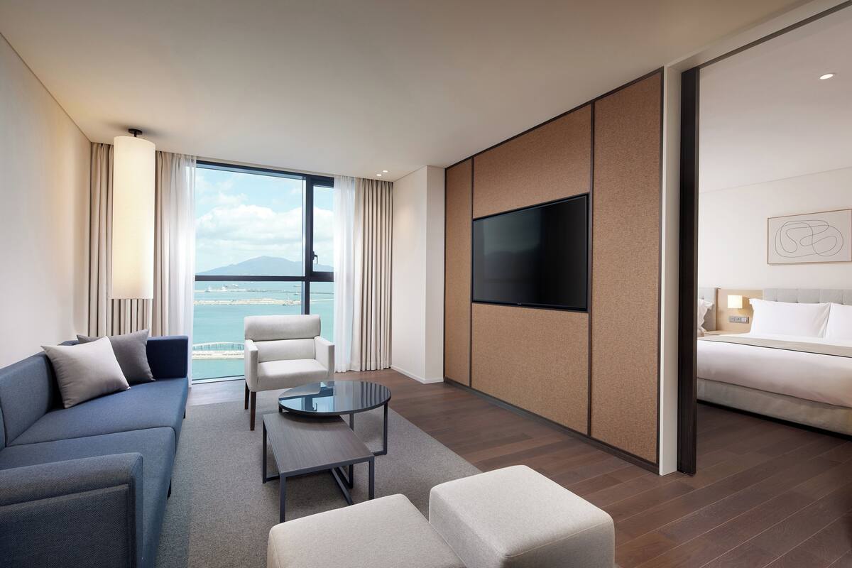 Quarto de hotel moderno com sofá, poltronas, mesa de centro, televisão e cama.