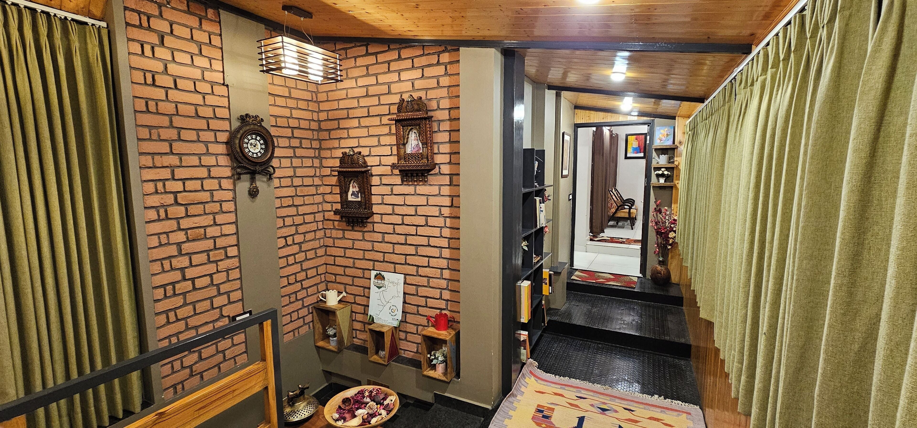 Um corredor estreito com paredes de tijolo, vigas de madeira e uma escadaria que leva a outro cômodo. Estantes com livros e objetos decorativos alinham as paredes.