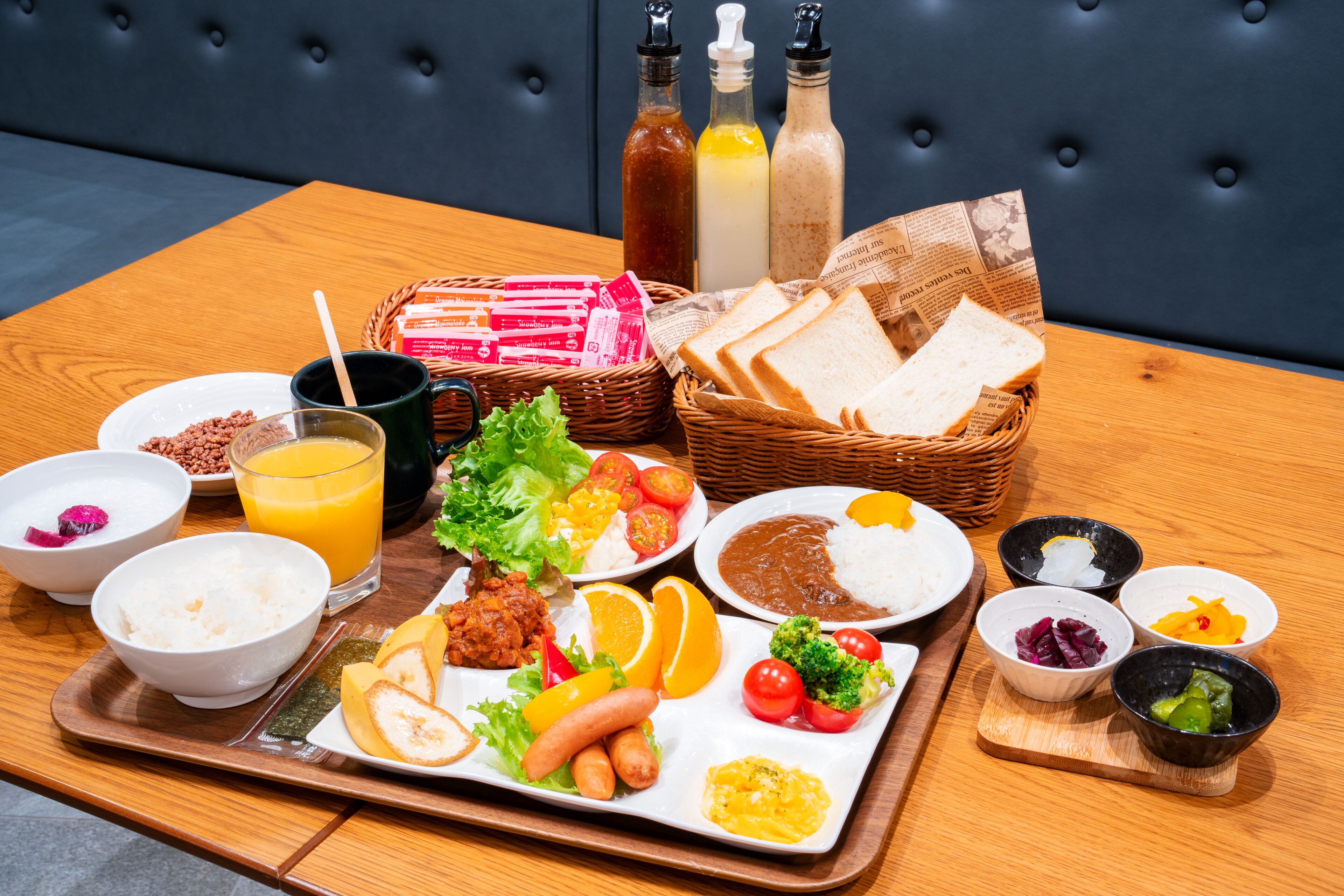 Bandeja de café da manhã com diversos pratos, incluindo arroz, ovos, linguiça e legumes, sobre uma mesa de madeira.