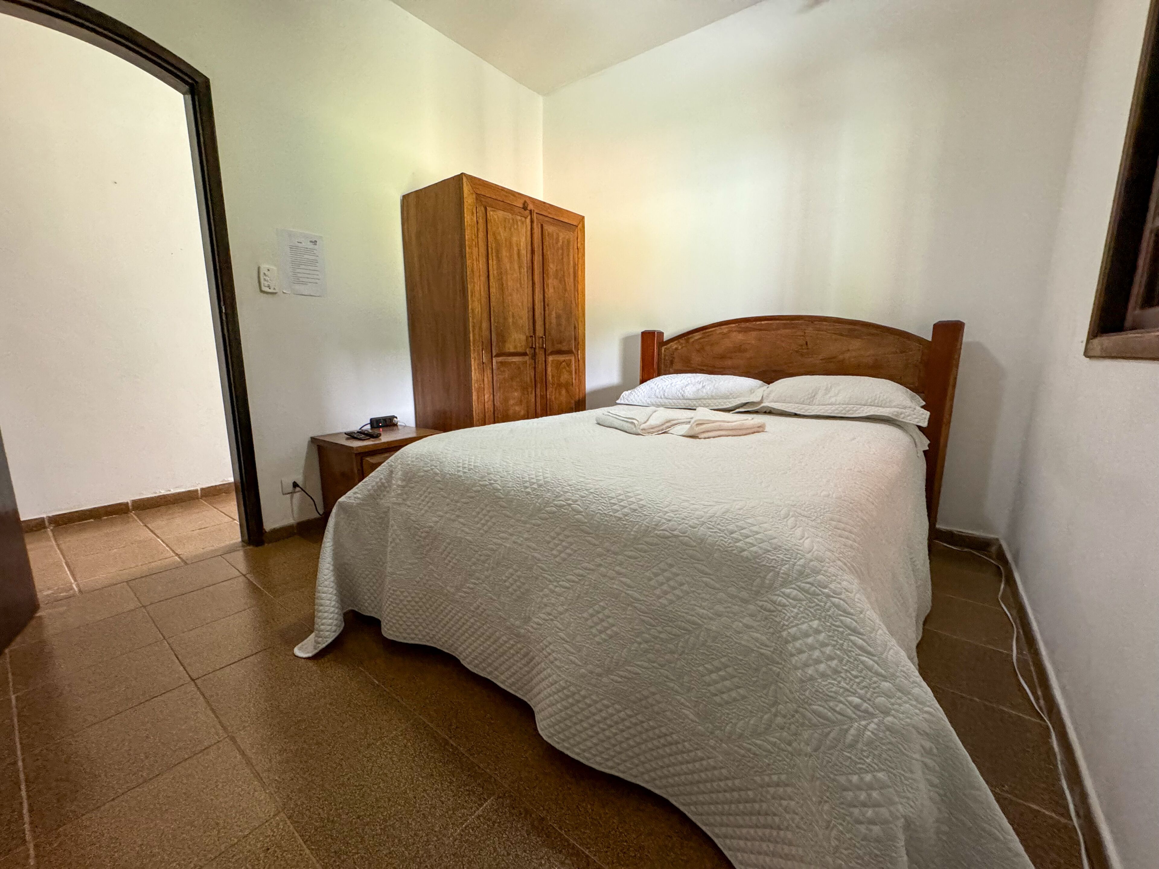 Quarto com cama, guarda-roupa de madeira e mesa de cabeceira.