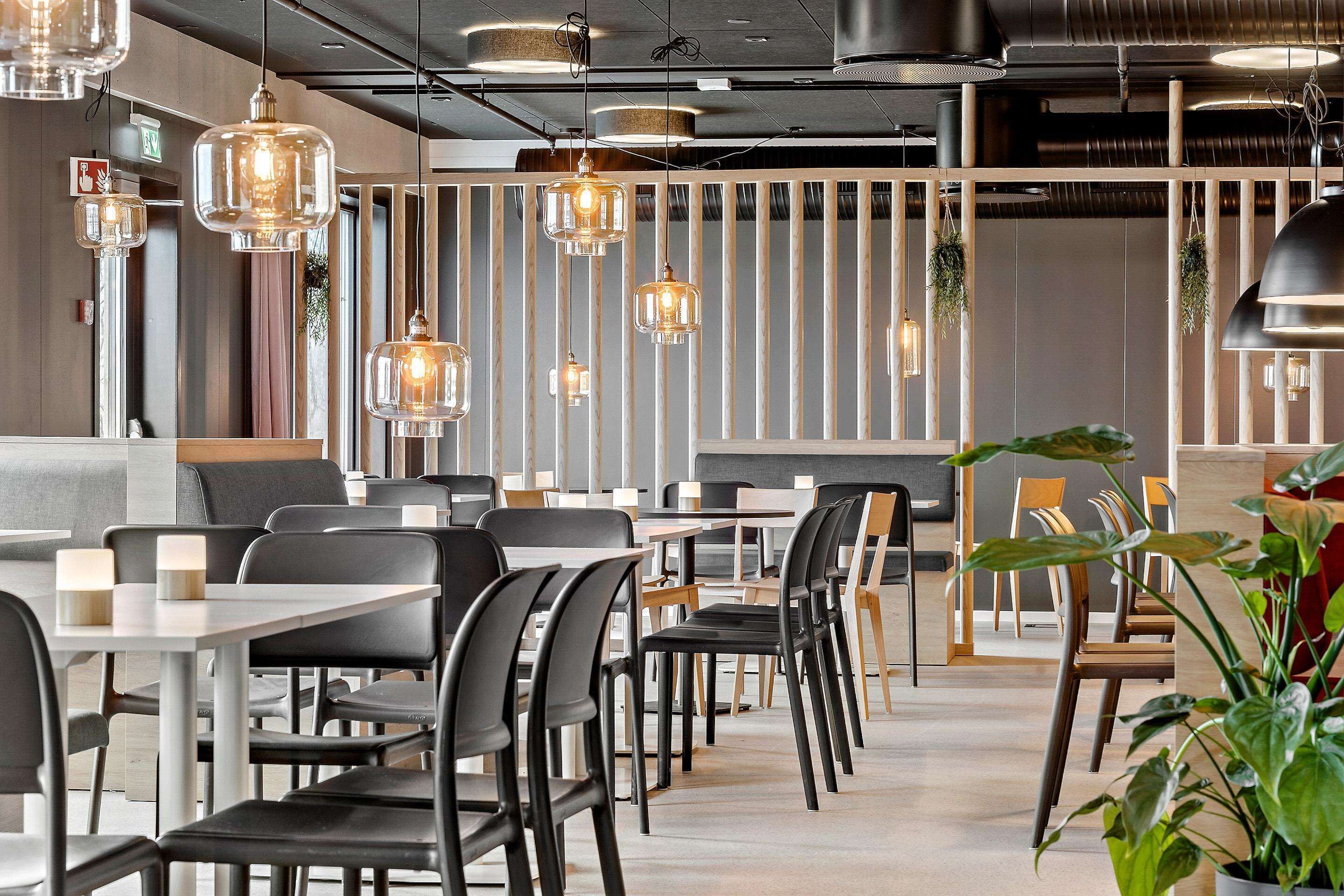 Interior moderno de restaurante com ripas de madeira, luminárias pendentes e cadeiras pretas.