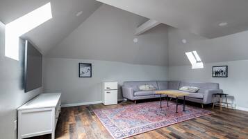 Quarto estilo loft com sofá cinza, escrivaninha branca pequena e tapete colorido.