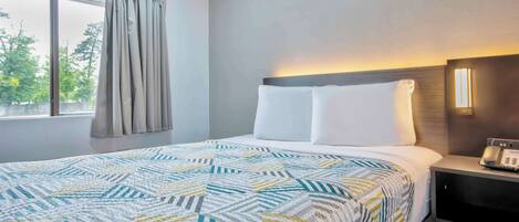 Quarto de hotel com uma cama grande, uma mesa de cabeceira com telefone e uma janela com cortinas.