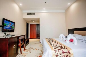 Quarto de hotel com uma cama, uma escrivaninha, uma televisão e uma porta que dá para outro quarto.