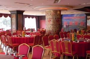 Uma sala de banquetes com mesas redondas e cadeiras, um pilar grande e um banner com texto.