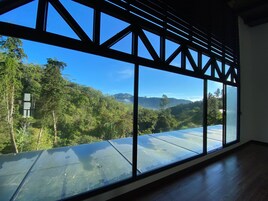 Quarto com amplas janelas que oferecem vista para uma encosta arborizada.