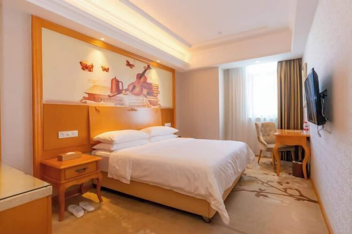 Quarto de hotel com uma cama grande, uma escrivaninha, uma cadeira e uma televisão.