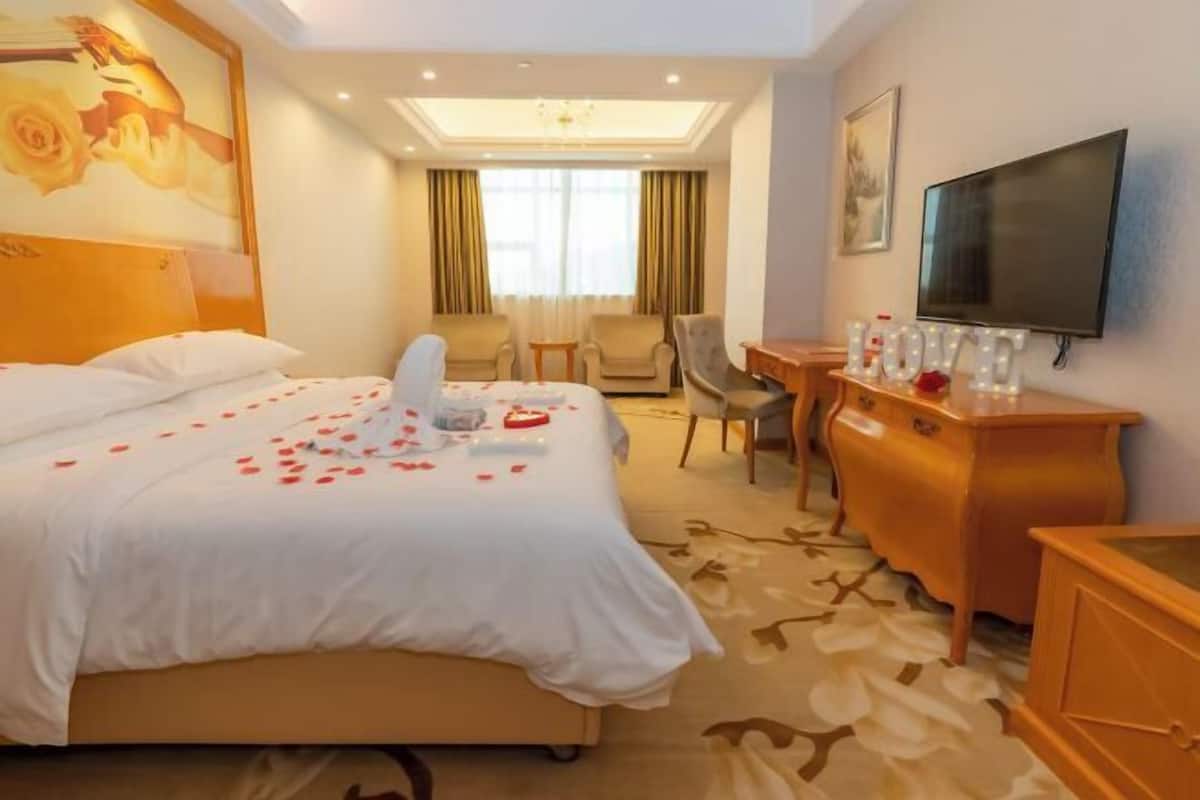 Quarto de hotel com cama, escrivaninha, televisão e um quadro na parede.