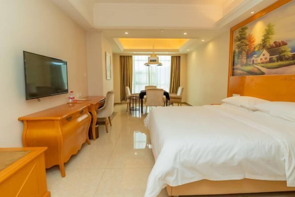 Quarto de hotel com cama, escrivaninha, televisão e um quadro na parede.