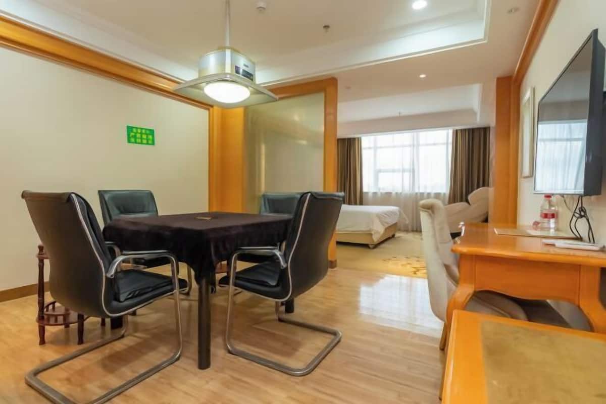Quarto de hotel com mesa de jantar, quatro cadeiras, uma cama, televisão e piso de madeira.