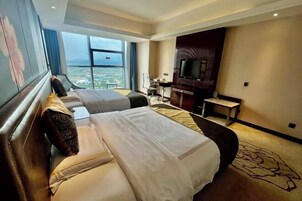 Quarto de hotel com duas camas, uma escrivaninha, uma cadeira, uma televisão e uma janela grande com vista para a cidade.