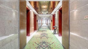 Um corredor de hotel com carpete estampado, painéis de madeira e paredes de mármore.