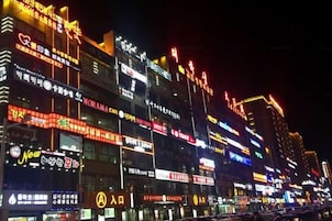 Rua urbana iluminada à noite, com letreiros e edifícios com luzes.