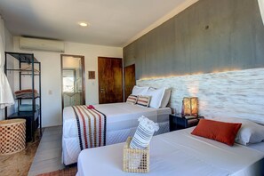 Quarto de hotel com duas camas, um guarda-roupa, um espelho e uma mesa de cabeceira com abajur.