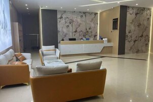 Um saguão de hotel com balcão de recepção, área de estar e parede de mármore.