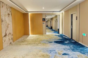 Corredor de hotel com carpete azul, paredes bege e portas que dão para os quartos.