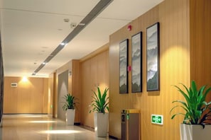 Um saguão de hotel com painéis de madeira, plantas em vasos e quadros nas paredes.