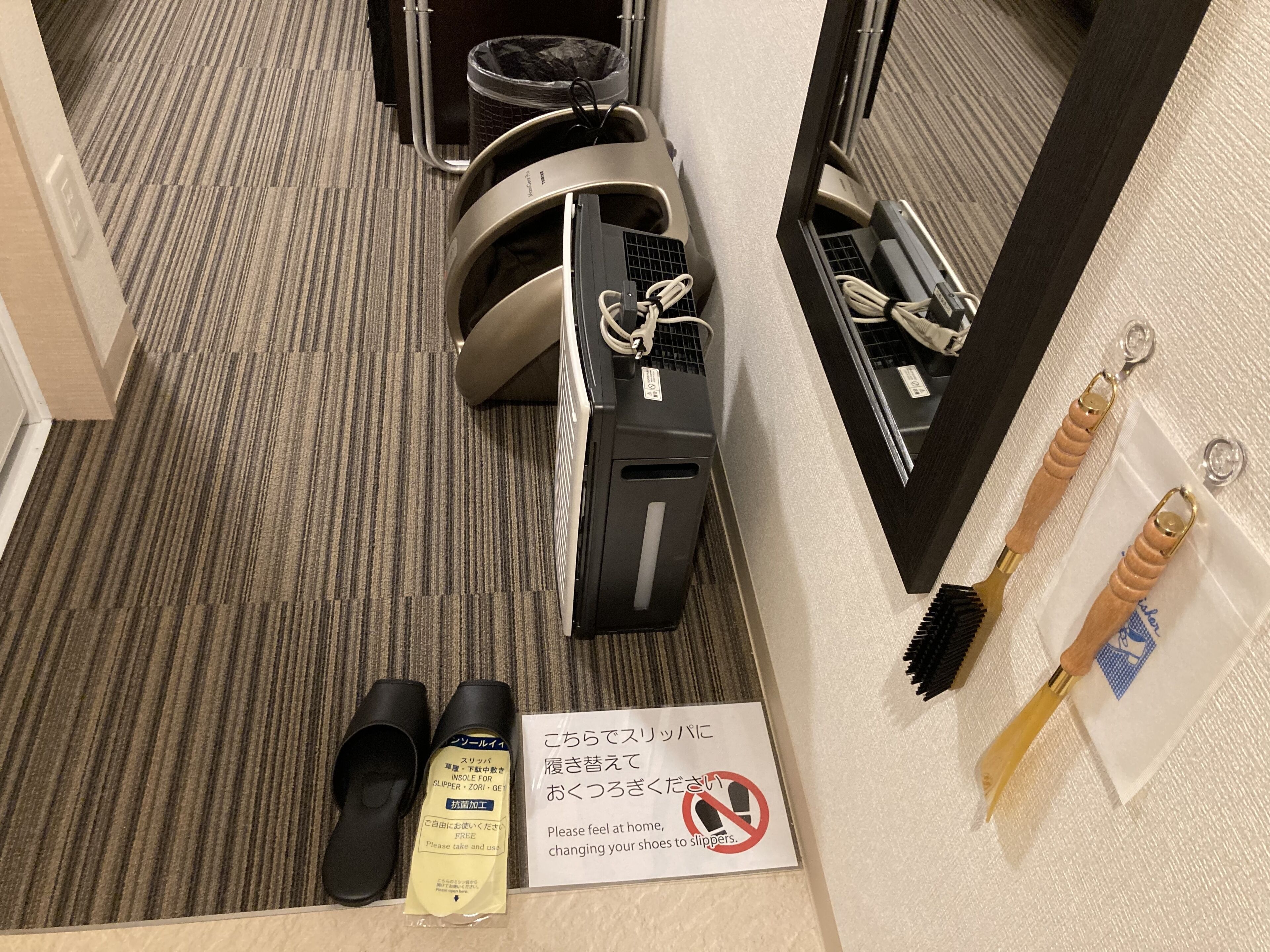 Quarto de hotel com um espaço para engraxar sapatos, chinelos e um aviso solicitando aos hóspedes que usem chinelos.