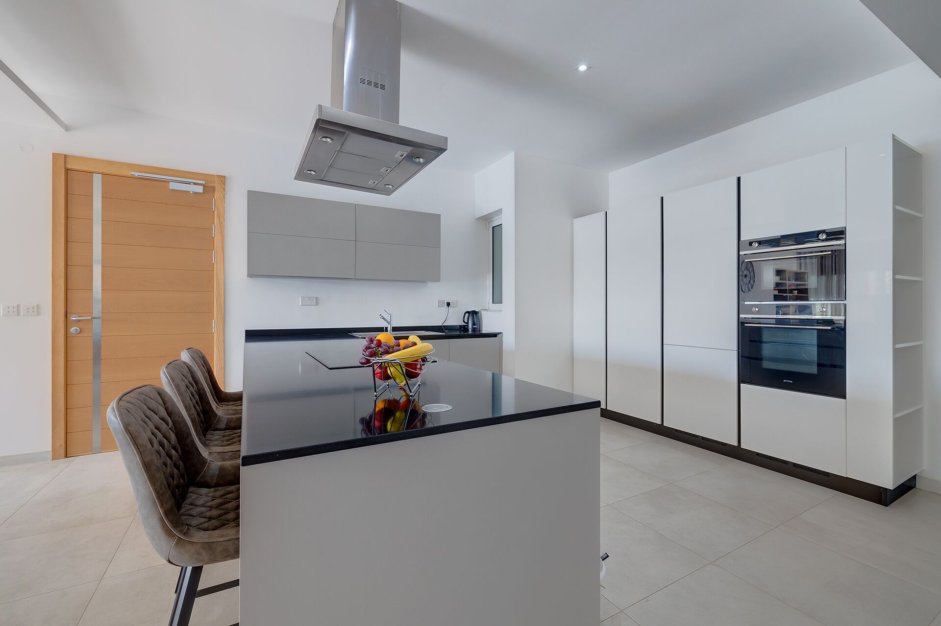 Uma cozinha moderna com ilha central, armários brancos e eletrodomésticos embutidos.