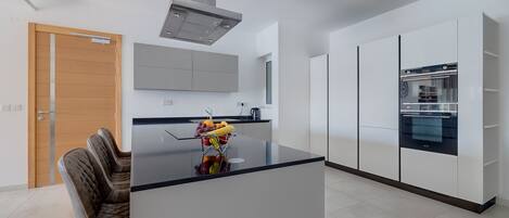 Uma cozinha moderna com ilha central, armários brancos e eletrodomésticos embutidos.