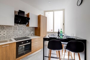 Cozinha moderna com forno embutido, fogão e pia. Existe uma área de jantar com duas cadeiras e uma mesa posta para dois.