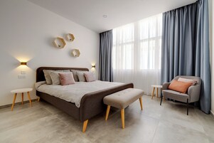 Quarto moderno com uma cama grande, um banco, uma cadeira e uma mesa pequena.