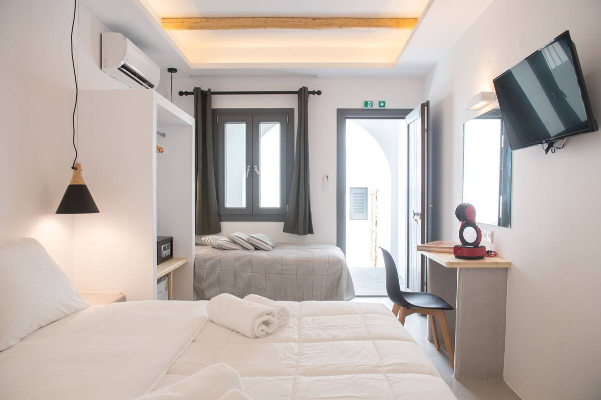 Quarto de hotel com cama, escrivaninha, cadeira, televisão e ar condicionado.