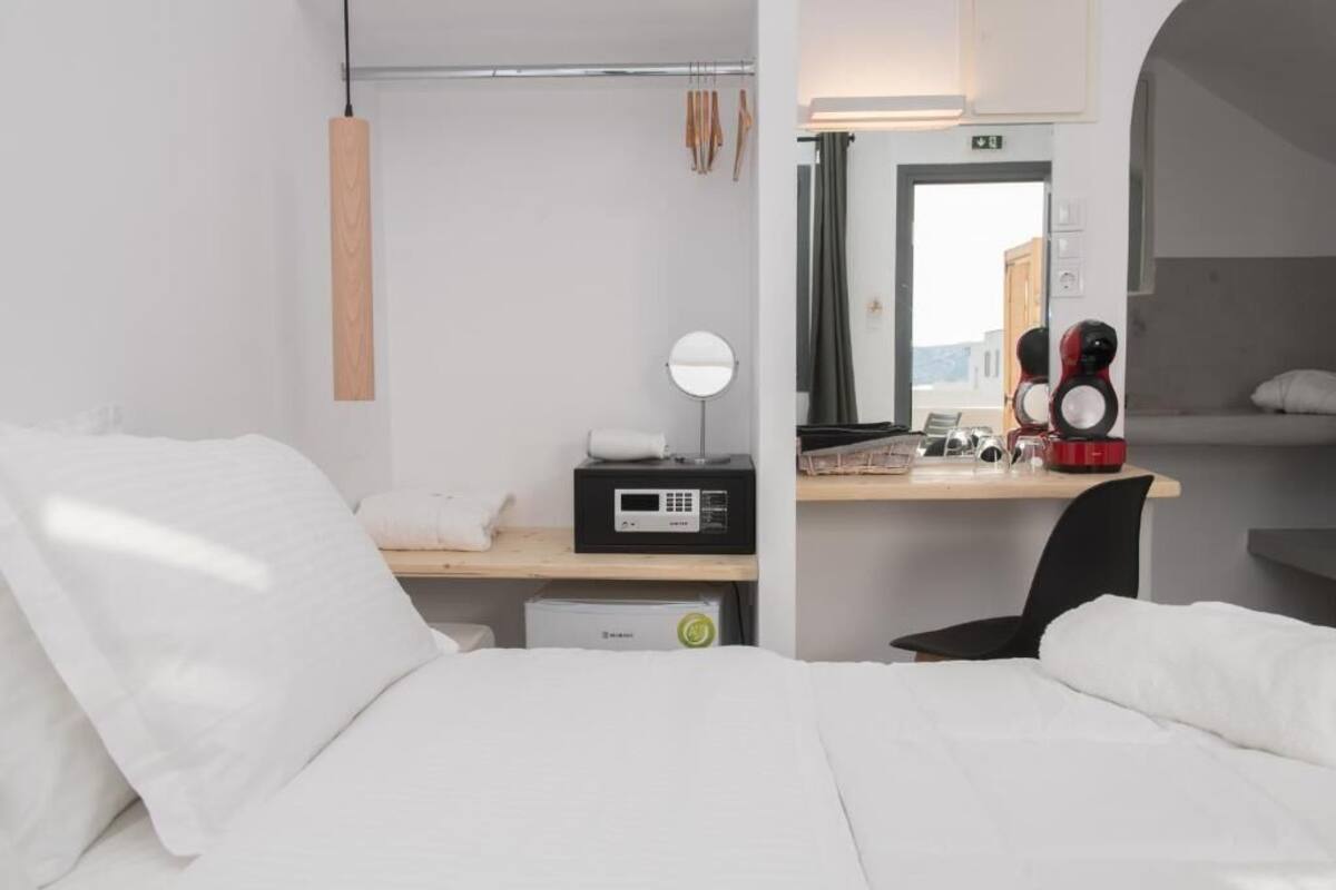 Quarto de hotel com uma cama, uma escrivaninha com um rádio, um espelho e vista para a cidade pela janela.