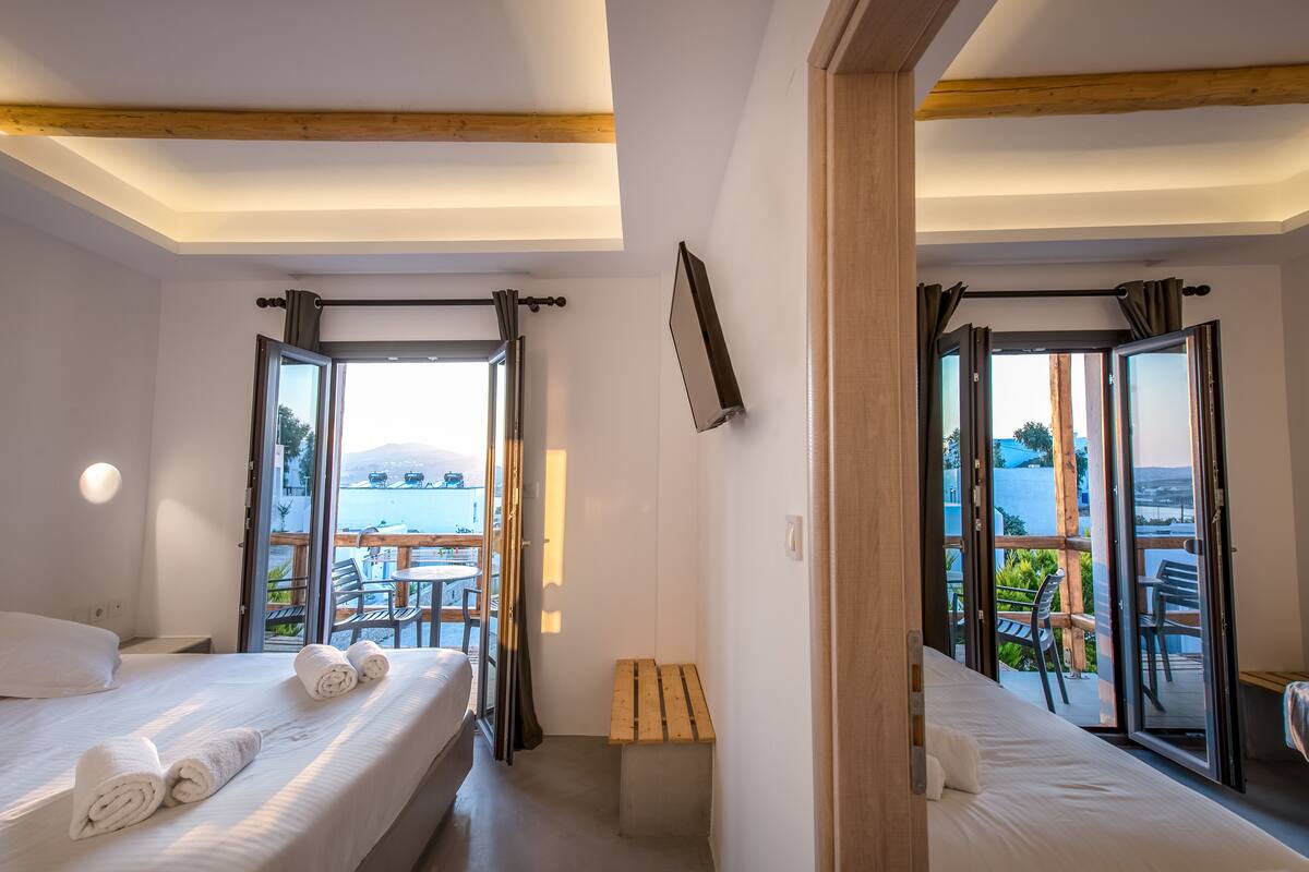 Quarto de hotel com duas camas, um banco de madeira e vista para o mar.