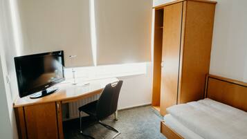 Quarto de hotel com escrivaninha de madeira, cadeira preta, cama e guarda-roupa.