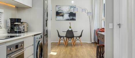 Cozinha moderna com máquina de lavar, área de jantar com mesa e cadeiras, e um grande quadro abstrato na parede.