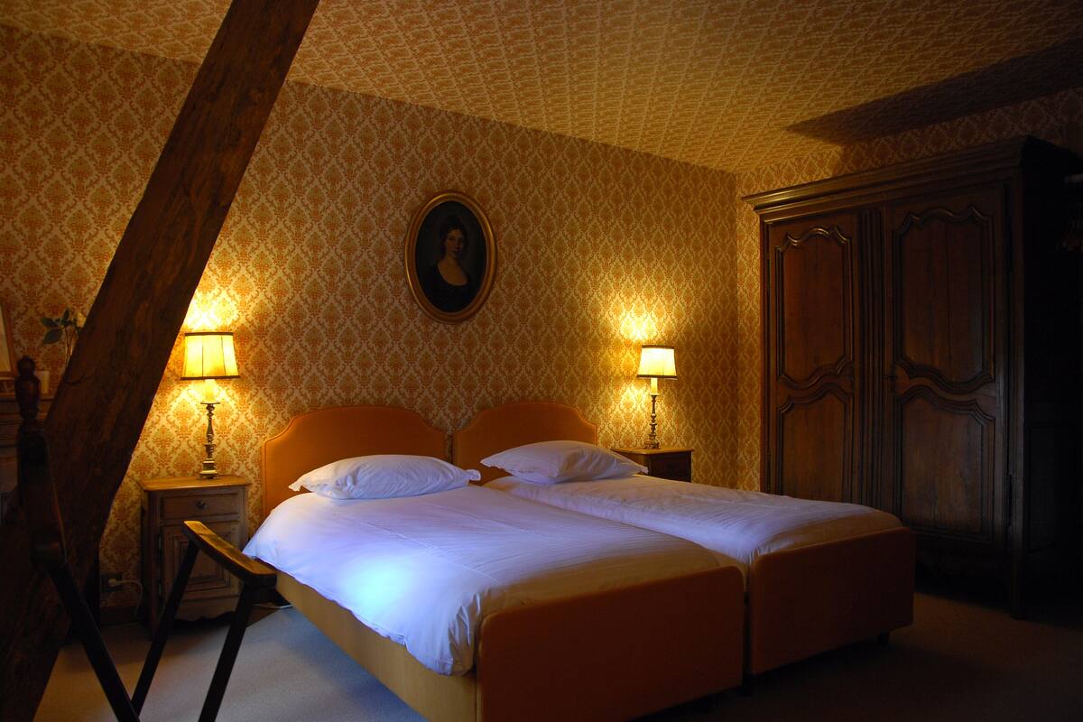 Quarto com uma cama de casal, duas mesas de cabeceira com luminárias, um guarda-roupa de madeira e um papel de parede estampado.