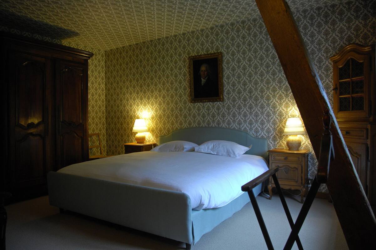 Quarto com uma cama grande, duas mesas de cabeceira com luminárias, um guarda-roupa de madeira e um papel de parede estampado.