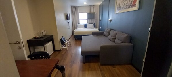 Quarto de hotel compacto com cama, sofá, escrivaninha e cadeira.