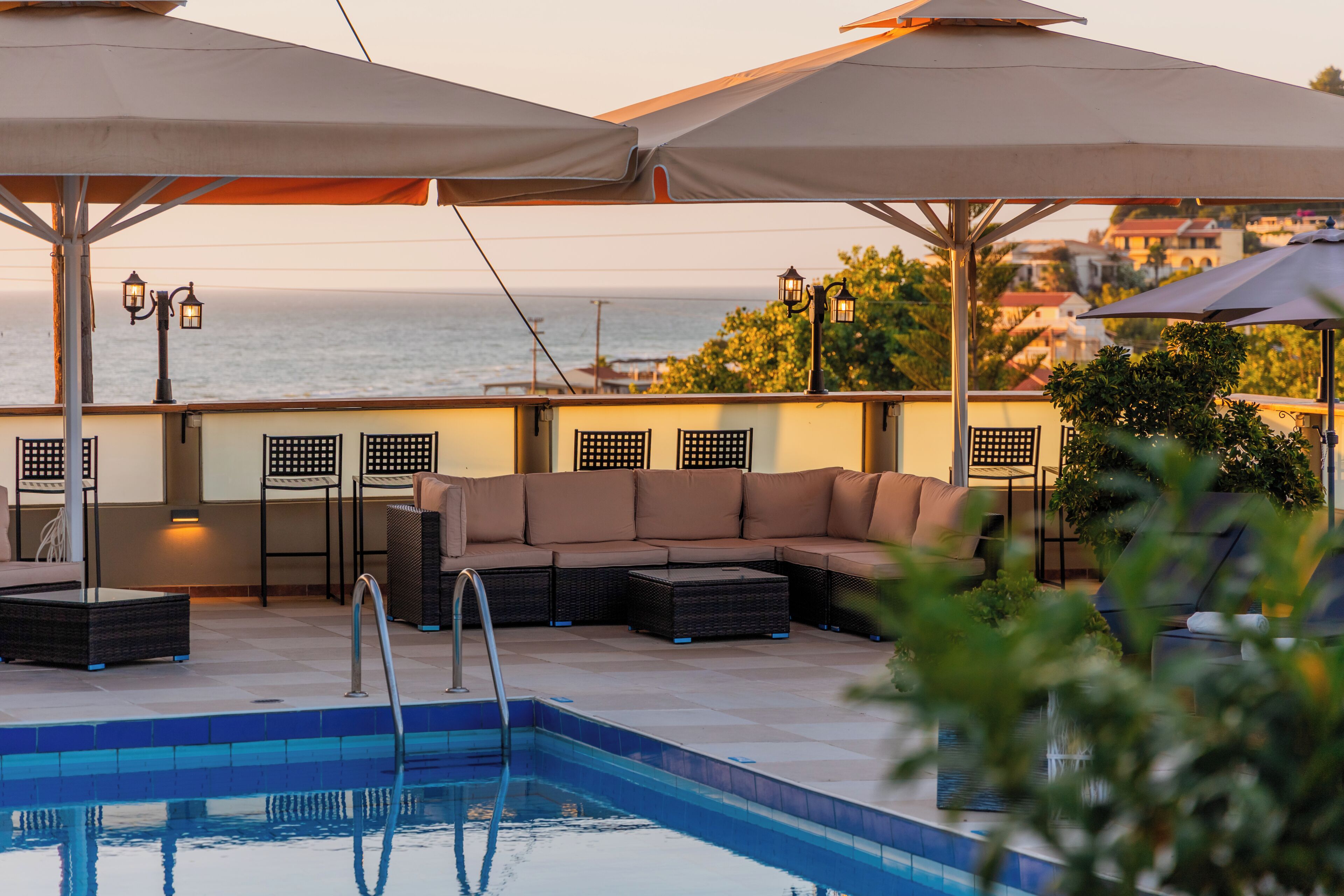 Uma área junto à piscina com sofás, cadeiras e guarda-sóis, com vista para o mar.