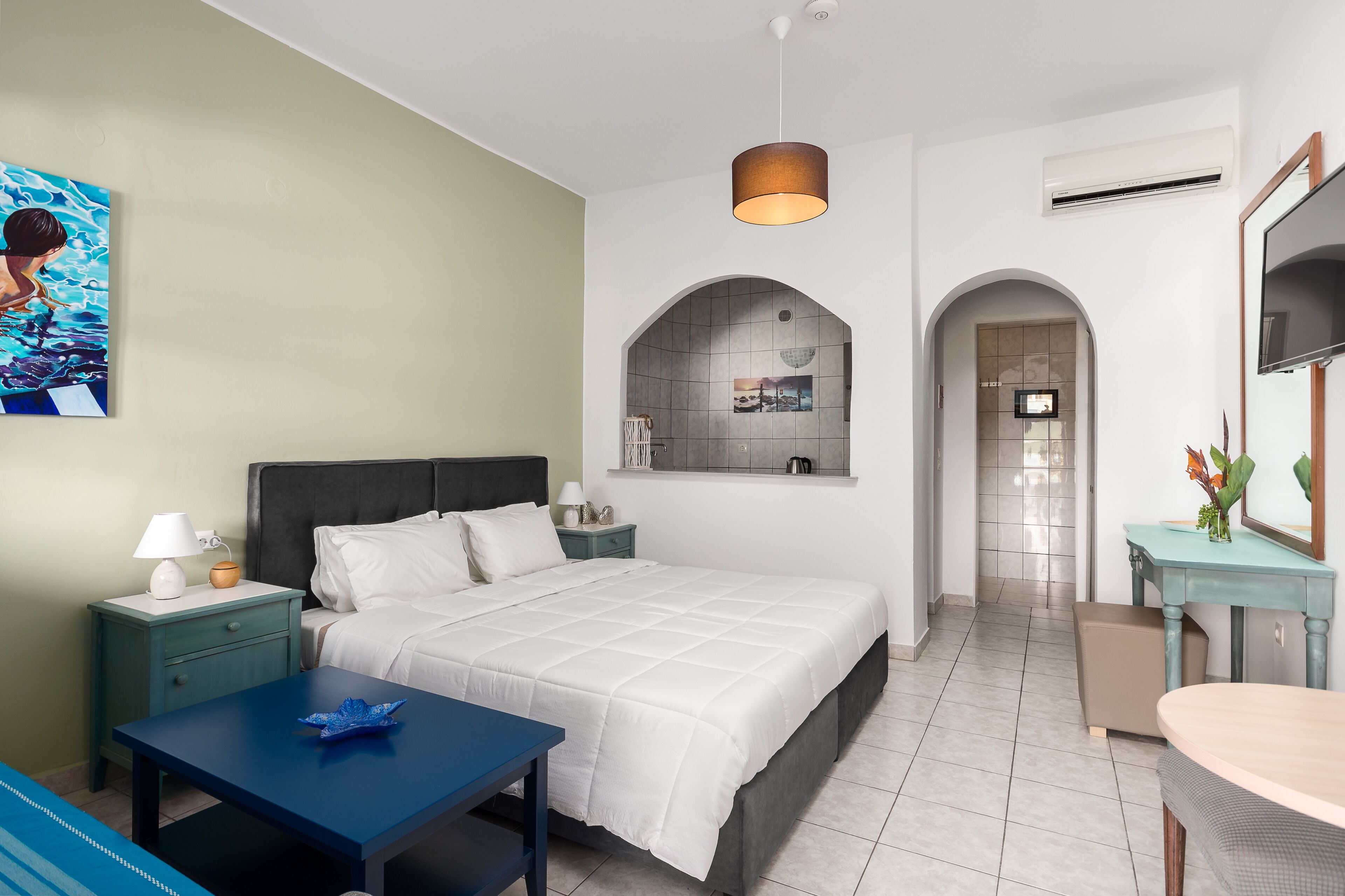 Quarto de hotel com cama, mesa de cabeceira, luminária e um quadro na parede.