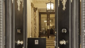 Uma entrada imponente com portas negras ornamentadas, piso xadrez e um candelabro.