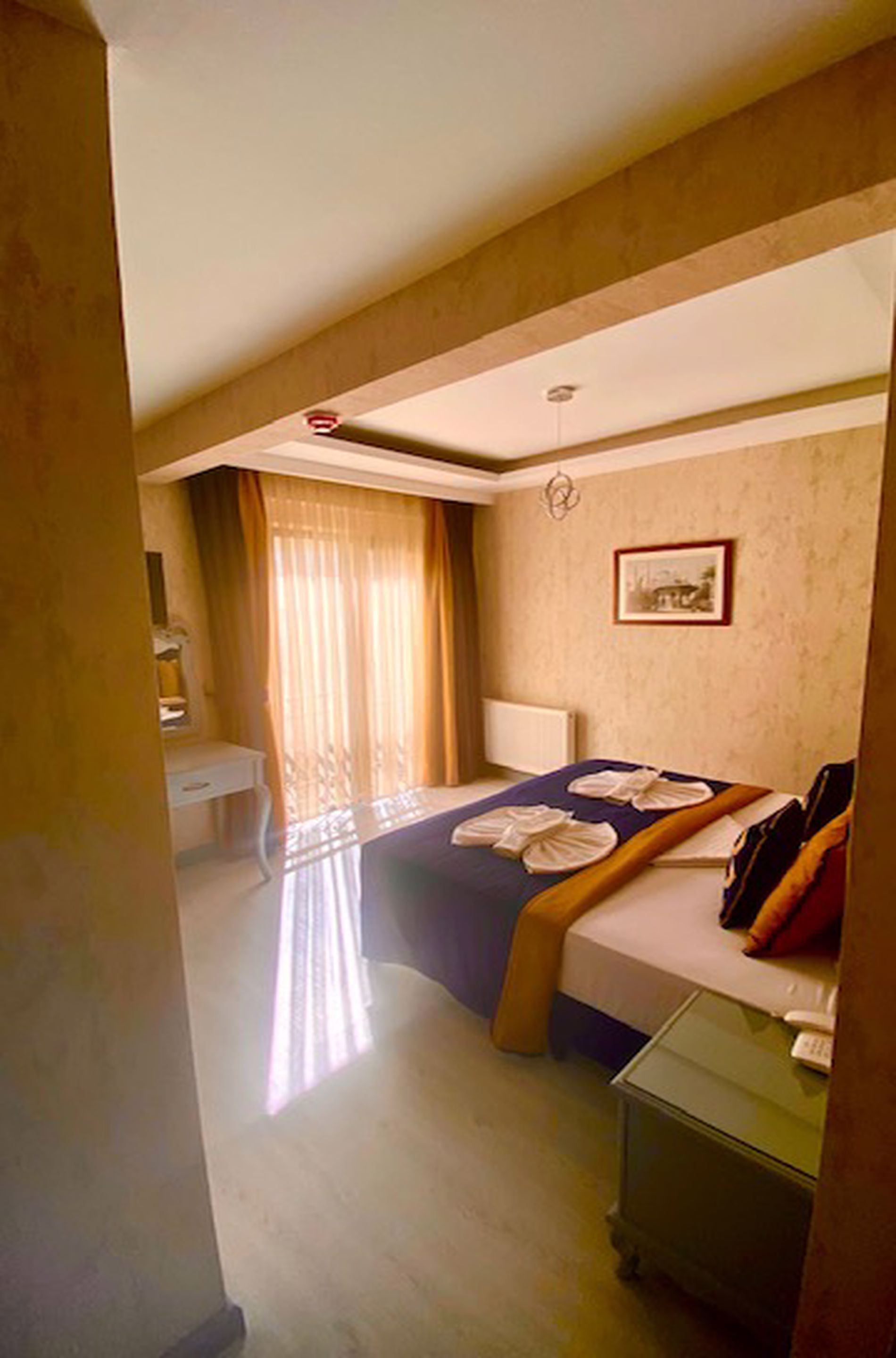 Quarto de hotel com uma cama, mesa de cabeceira e janela com cortinas.