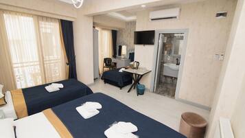 Quarto de hotel com duas camas, uma mesa, uma cadeira, uma televisão, banheiro e lixeira.