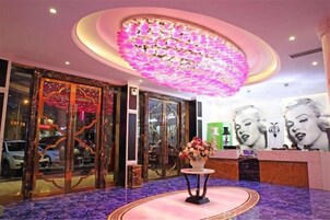 Um saguão de hotel com balcão de recepção, um lustre grande e uma parede com um mural de retrato.