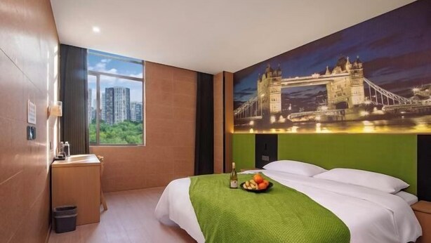 Quarto de hotel com cama, escrivaninha, lixeira, garrafa de vinho e uma cesta de frutas.