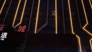 Fachada de prédio com linhas verticais iluminadas e sinalização indicando um local.