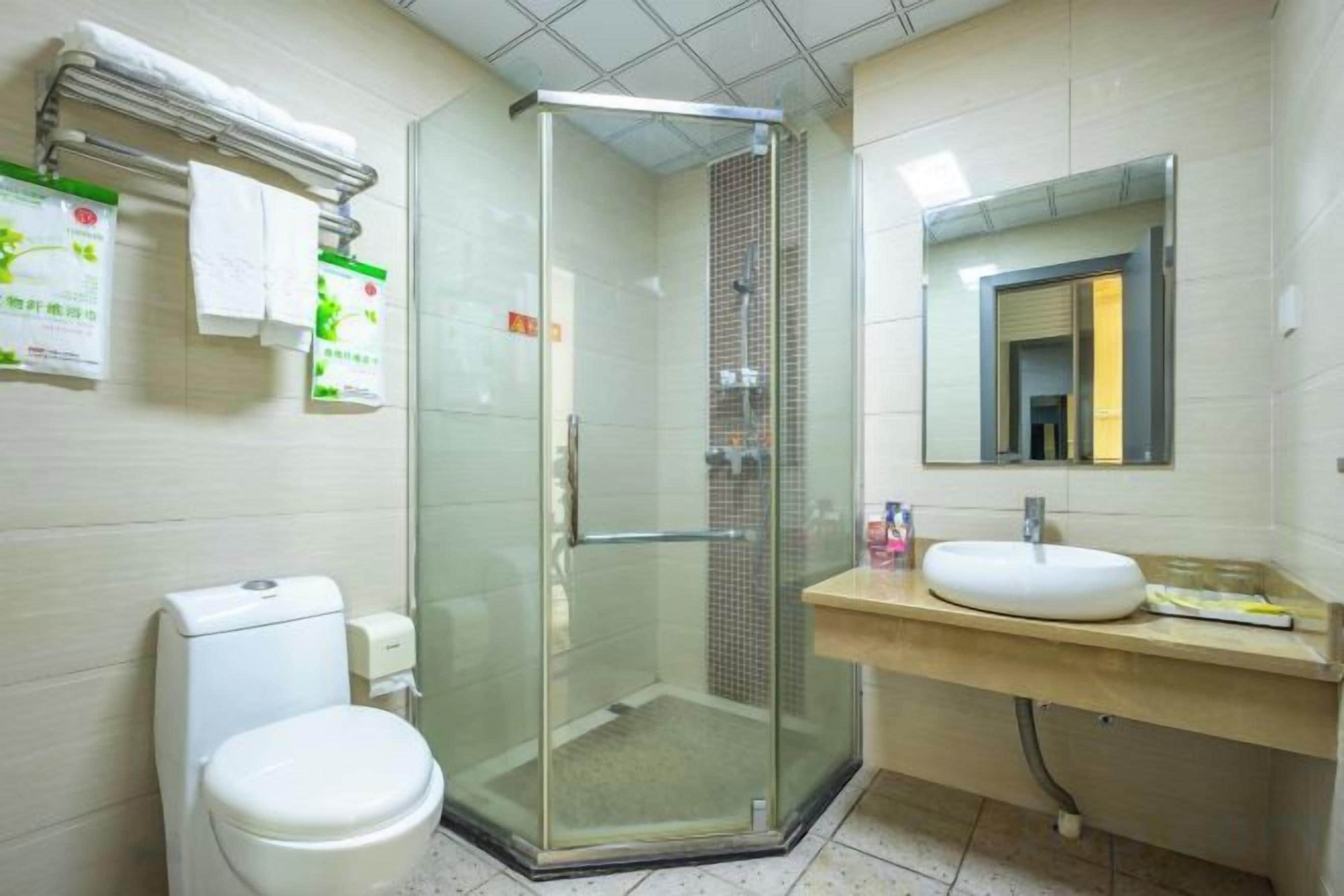 Casa de banho com cabine de chuveiro de vidro, sanita, lavatório e espelho.