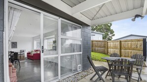 Alpendre coberto com porta de vidro deslizante que dá para uma sala de estar com sofá vermelho, mesa de jantar e cadeiras de exterior.