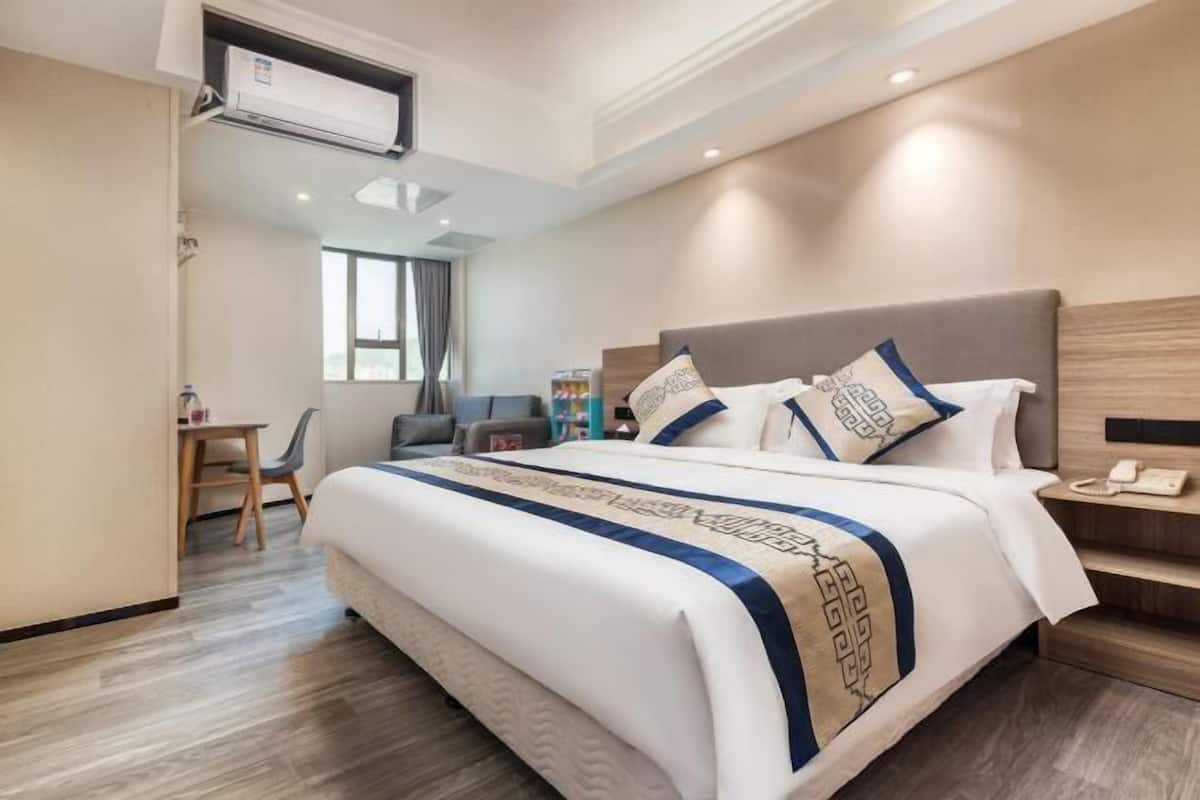 Quarto de hotel com uma cama grande, uma escrivaninha, uma cadeira e uma mesinha.