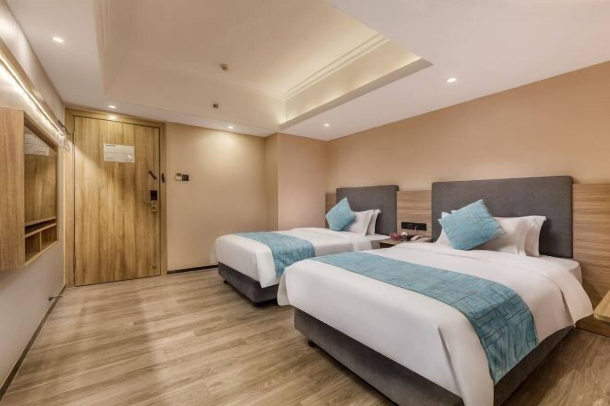 Quarto de hotel com duas camas, guarda-roupa de madeira e luminária no teto.
